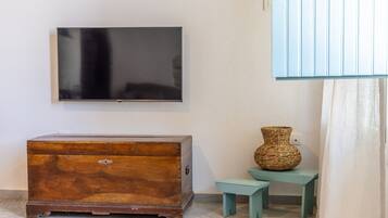 Quarto com uma cômoda de madeira, uma televisão de tela plana na parede, uma cesta de vime sobre um banquinho pequeno e um armário azul.
