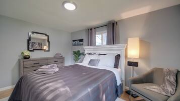 Quarto com cama, uma cadeira, mesa de cabeceira, luminária e janela com cortinas.