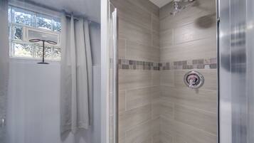 Chuveiro com porta de vidro, janela com cortinas e painel de azulejos.