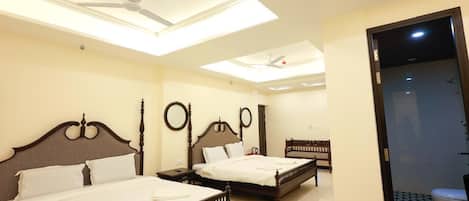 Quarto de hotel com duas camas, ventoinha no teto, claraboias e banheiro com piso estampado.