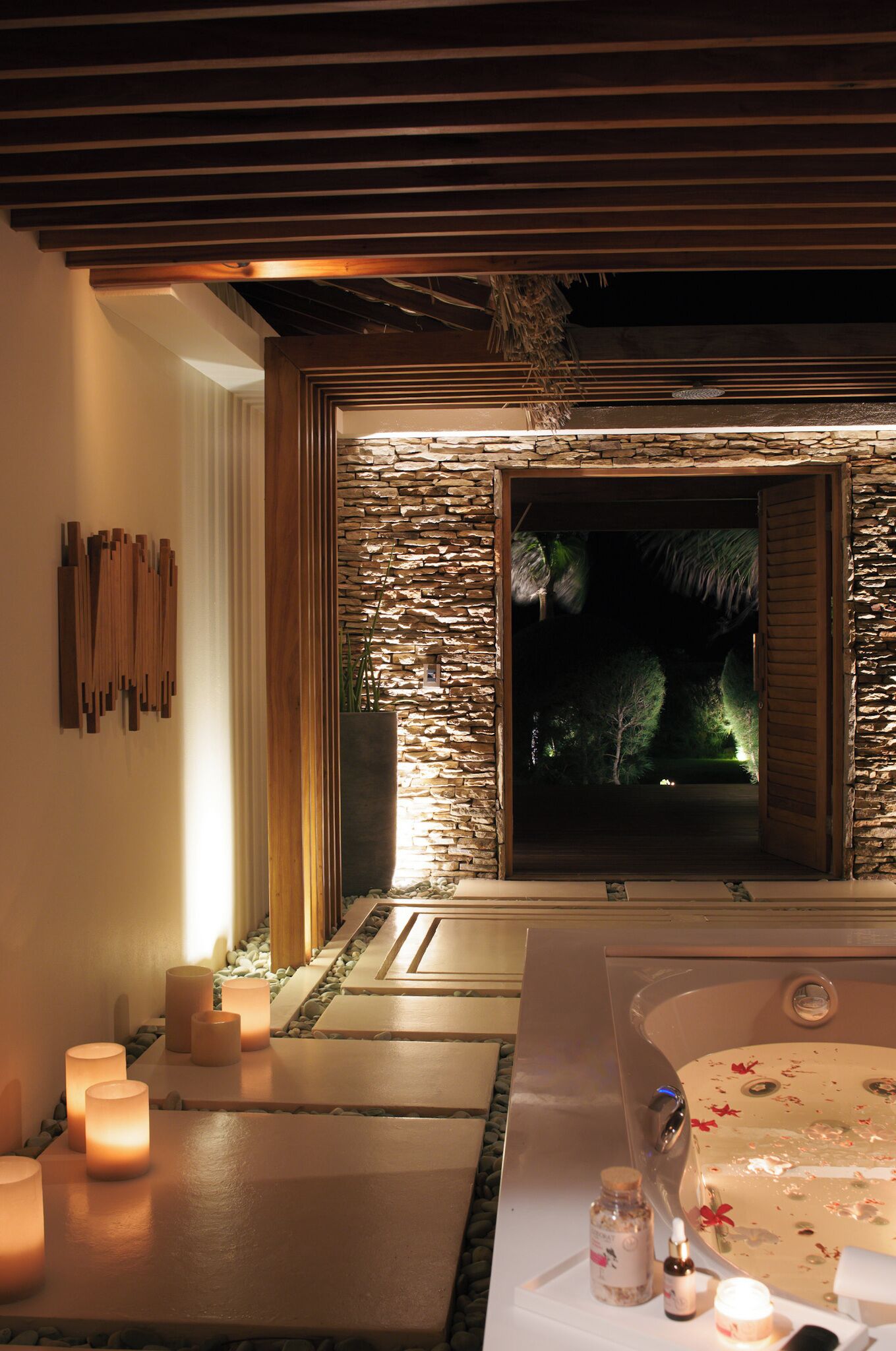 Uma área de spa com parede de pedra, banheira, velas e teto de madeira.