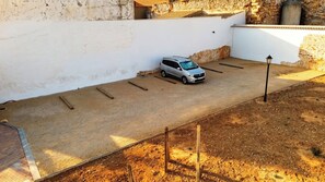 Uma área de estacionamento com uma parede branca e pavimento, um carro estacionado e um poste de luz.