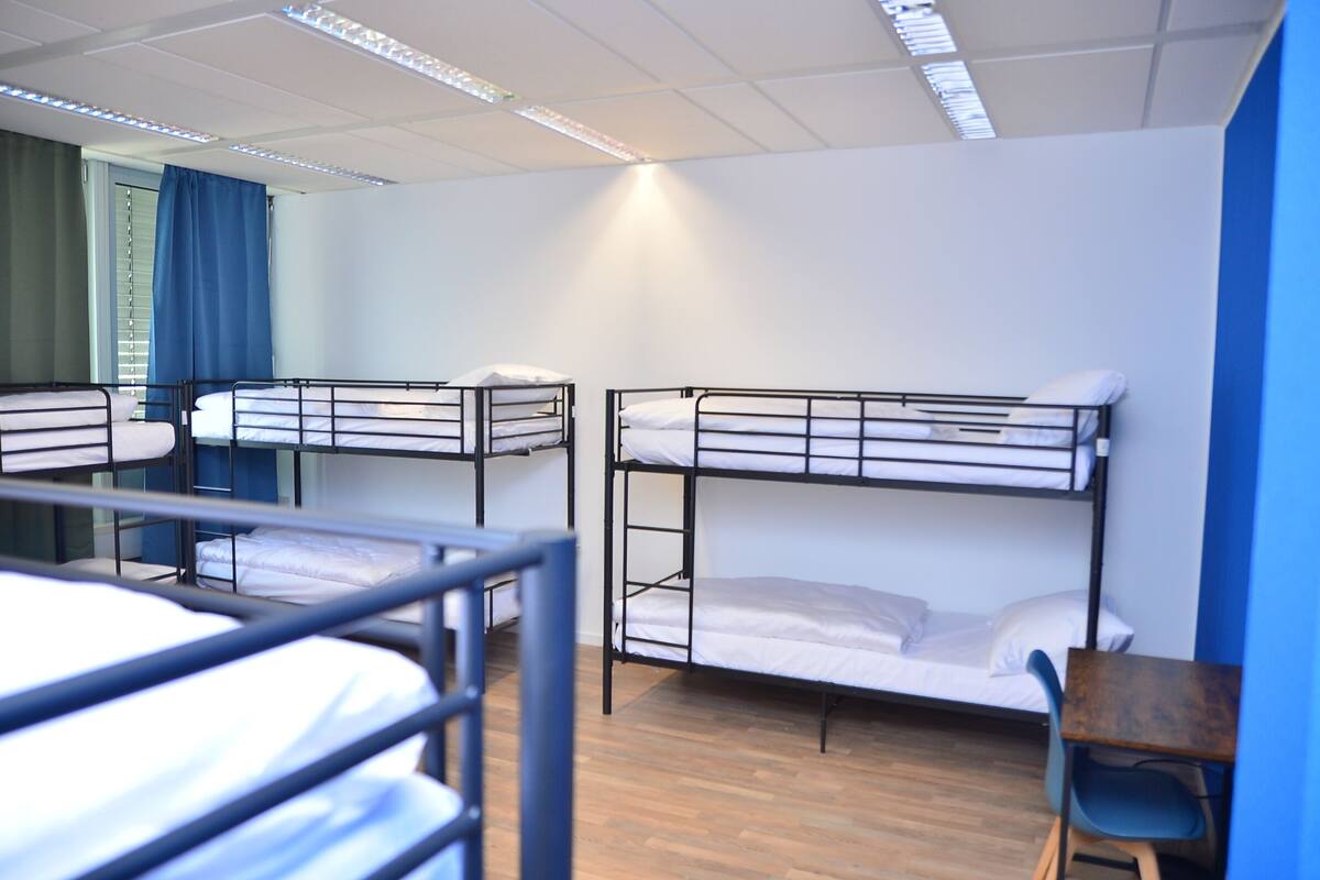 Um quarto de estudante com beliches, uma escrivaninha e uma cadeira.