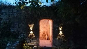 Um arco de pedra com uma porta de madeira, iluminado por duas luzes fixadas na parede.