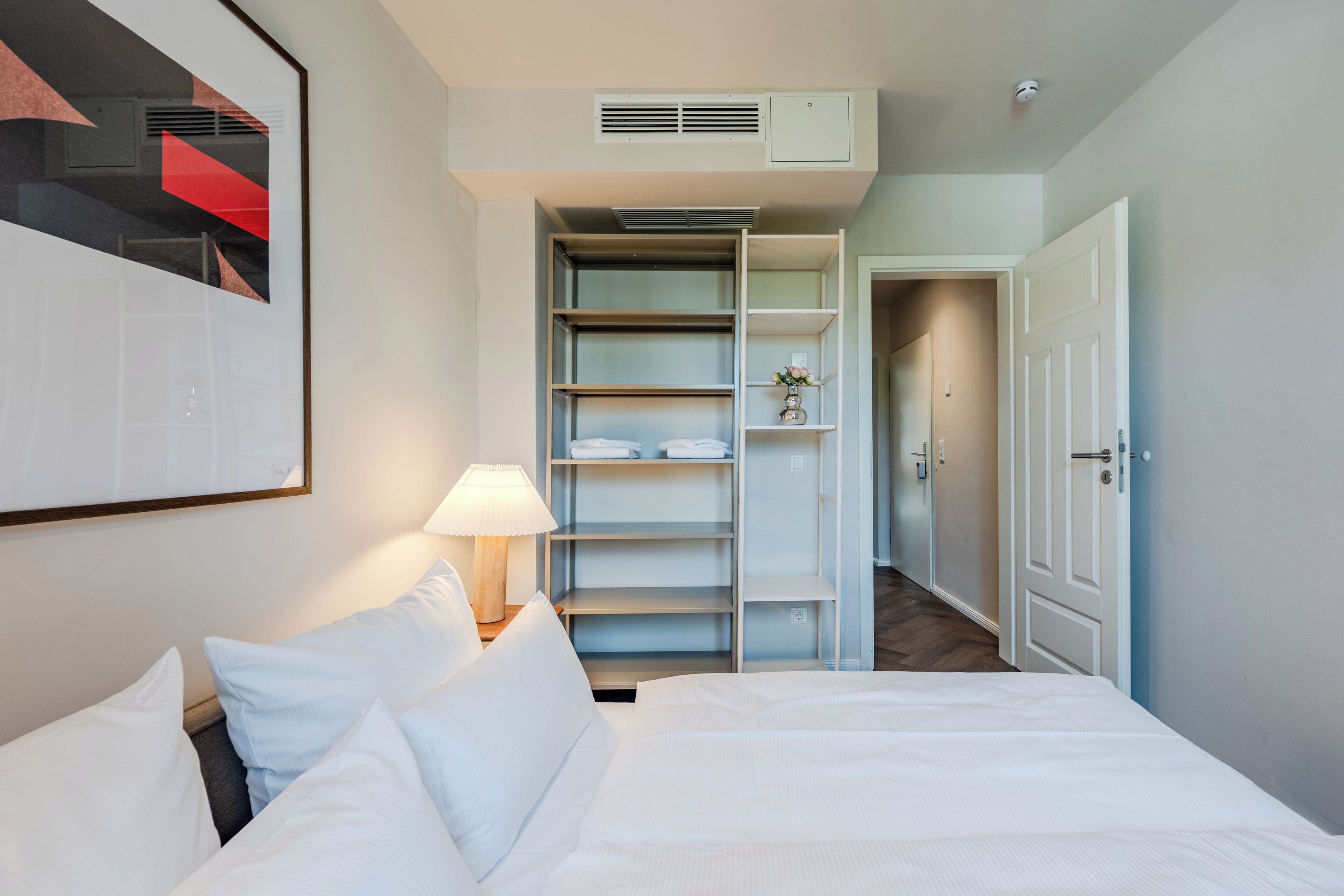 Quarto de hotel com uma cama, mesa de cabeceira, luminária, guarda-roupa e espelho.