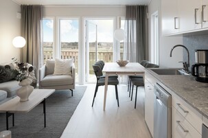 Uma sala de estar moderna com um sofá, uma mesa de jantar e uma área de cozinha equipada com lava-louças e cafeteira.