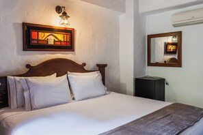 Uma cama bem arrumada com lençóis brancos, cabeceira de madeira e mesa de cabeceira com abajur.