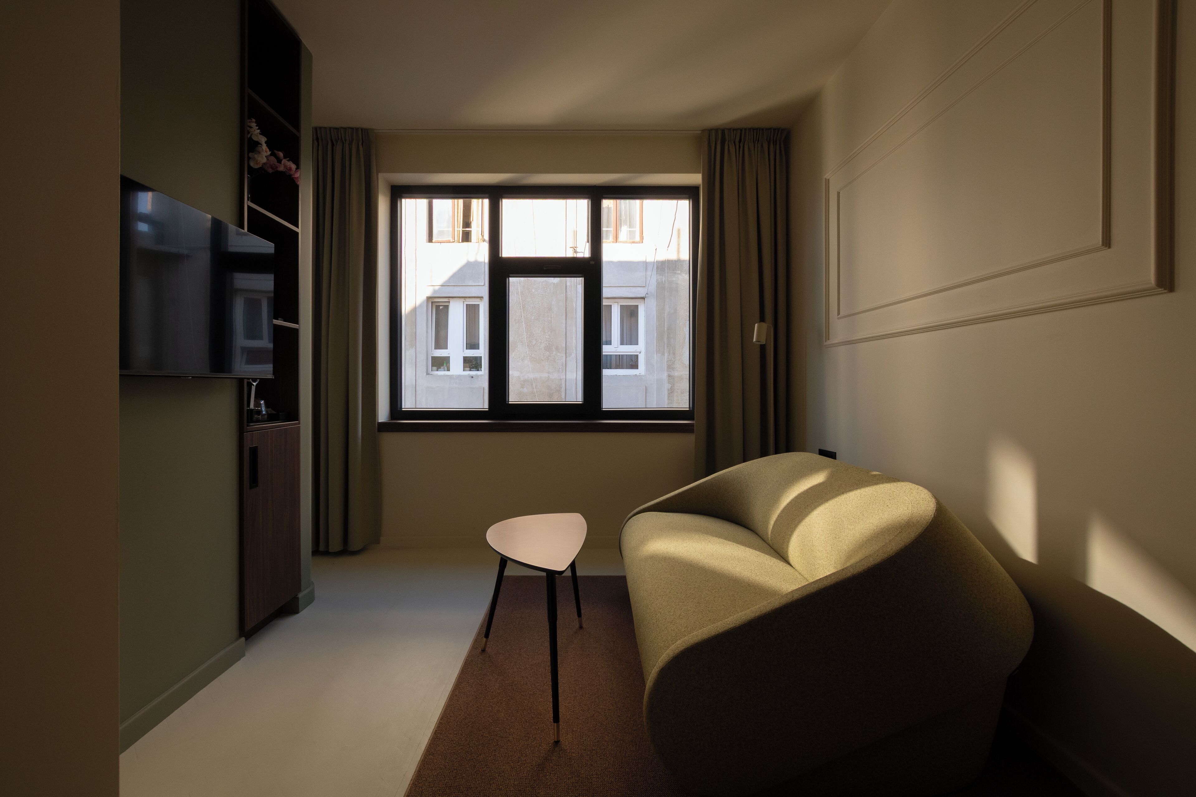 Uma sala de estar moderna com sofá, mesa pequena, TV de tela plana e janela com cortinas.