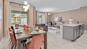 Cozinha moderna com ilha central, área de jantar com mesa posta para quatro e sala de estar com sofá e mesa de centro.