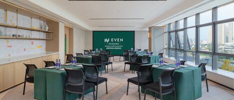 Sala de conferências com mesas, cadeiras e uma tela grande exibindo texto.
