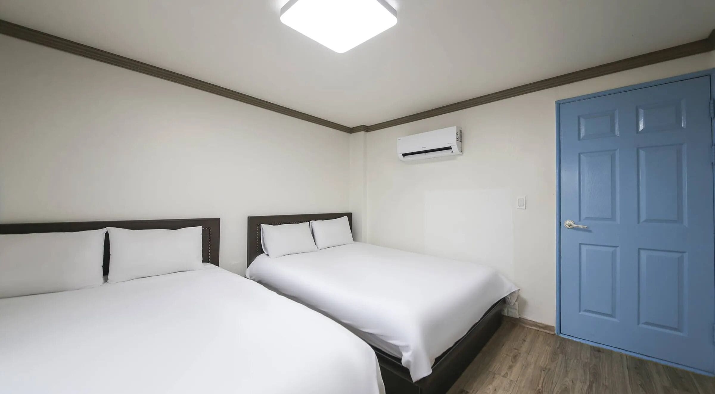 Quarto com duas camas, uma porta azul e um ar condicionado.