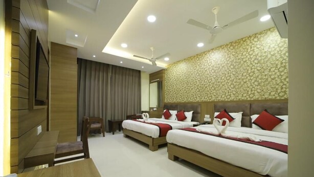 Quarto de hotel com duas camas, um banco de madeira, uma mesa e um ventilador de teto.