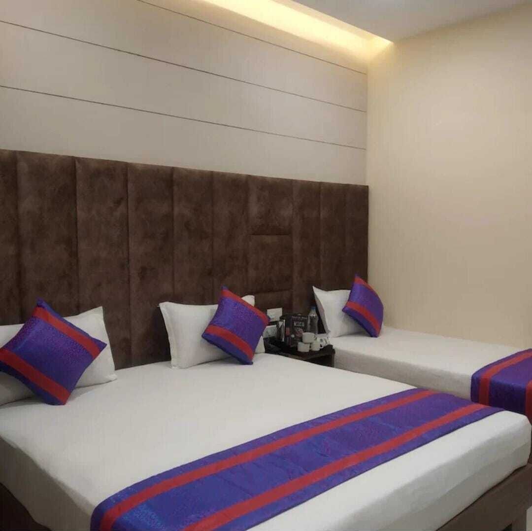 Quarto de hotel com duas camas, cada uma com roupa de cama branca e edredons listrados em roxo e vermelho.