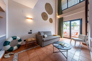Sala de estar moderna com um sofá cinzento, um banquinho de madeira, uma mesa de centro redonda e um tapete decorativo grande. Há duas luminárias fixadas na parede e três decorações de parede em tecido.