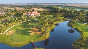 Um campo de golfe com um clube, lagoas e vegetação ao redor.
