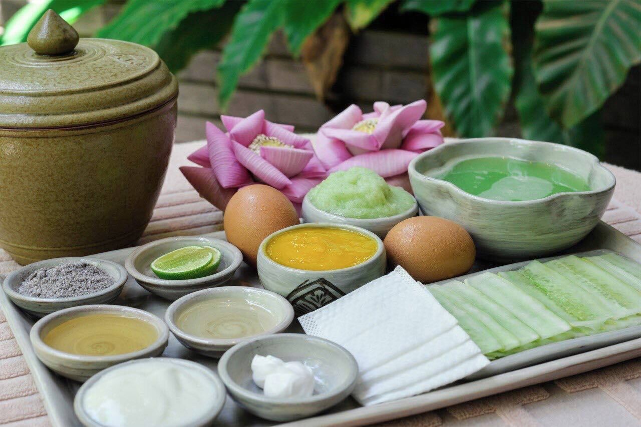 Uma bandeja com vários acompanhamentos, incluindo gomos de limão, ovos e diferentes molhos, disposta sobre uma mesa com um vaso decorativo e flores de lótus.
