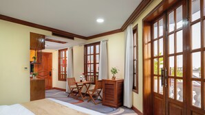Quarto de hotel com cama, escrivaninha, cadeiras e janela com cortinas.