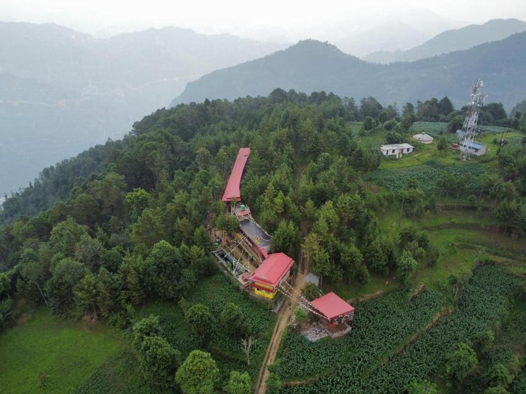 Paisagem montanhosa com um edifício de telhado vermelho e uma estrutura branca com torre.