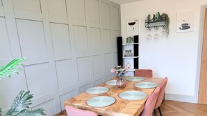 Uma área de refeições com uma mesa de madeira, cadeiras cor-de-rosa e um vaso com flores.