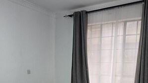Quarto com duas camas de solteiro, janela com cortinas e chão revestido de azulejos.
