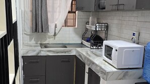 Cozinha compacta com armários escuros, bancada branca, micro-ondas e dispenser de água.