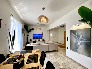 Uma sala de estar moderna com televisão, sofá, mesa de jantar e uma grande obra de arte.