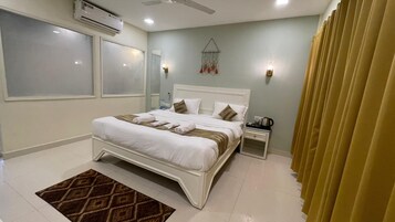 Quarto de hotel com cama, mesa de cabeceira, ar condicionado e janela com cortinas.