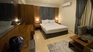 Quarto de hotel com cama, mesas de cabeceira, televisão, escrivaninha e sofá.