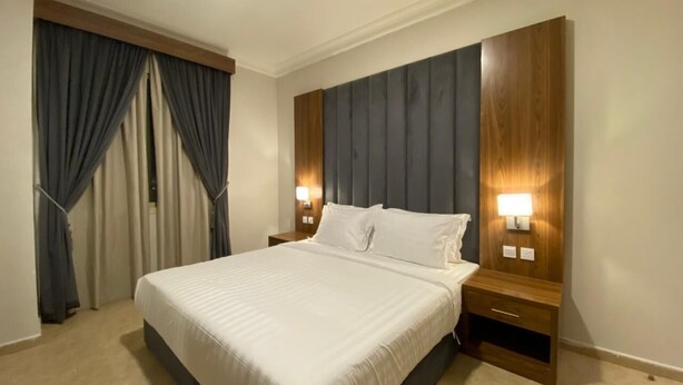 Quarto de hotel moderno com uma cama grande, cabeceira de madeira e abajures.