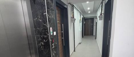 Corredor com elevadores e portas, piso de azulejos e parede branca.