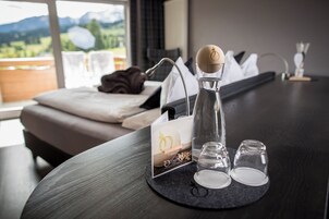 Quarto de hotel com uma cama, uma mesa com garrafa e copos, e vista para montanhas pela janela.