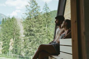 Um casal sentado em um banco de madeira perto de uma janela com vista para uma área arborizada.