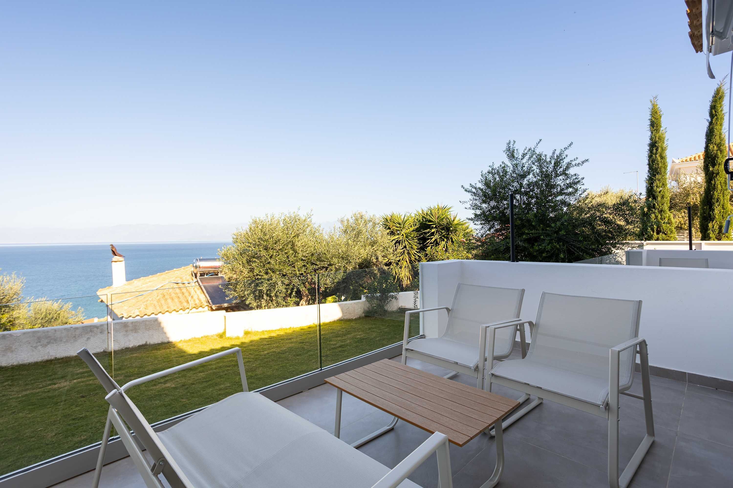 Um terraço com vista para o mar, uma mesa e duas cadeiras brancas.