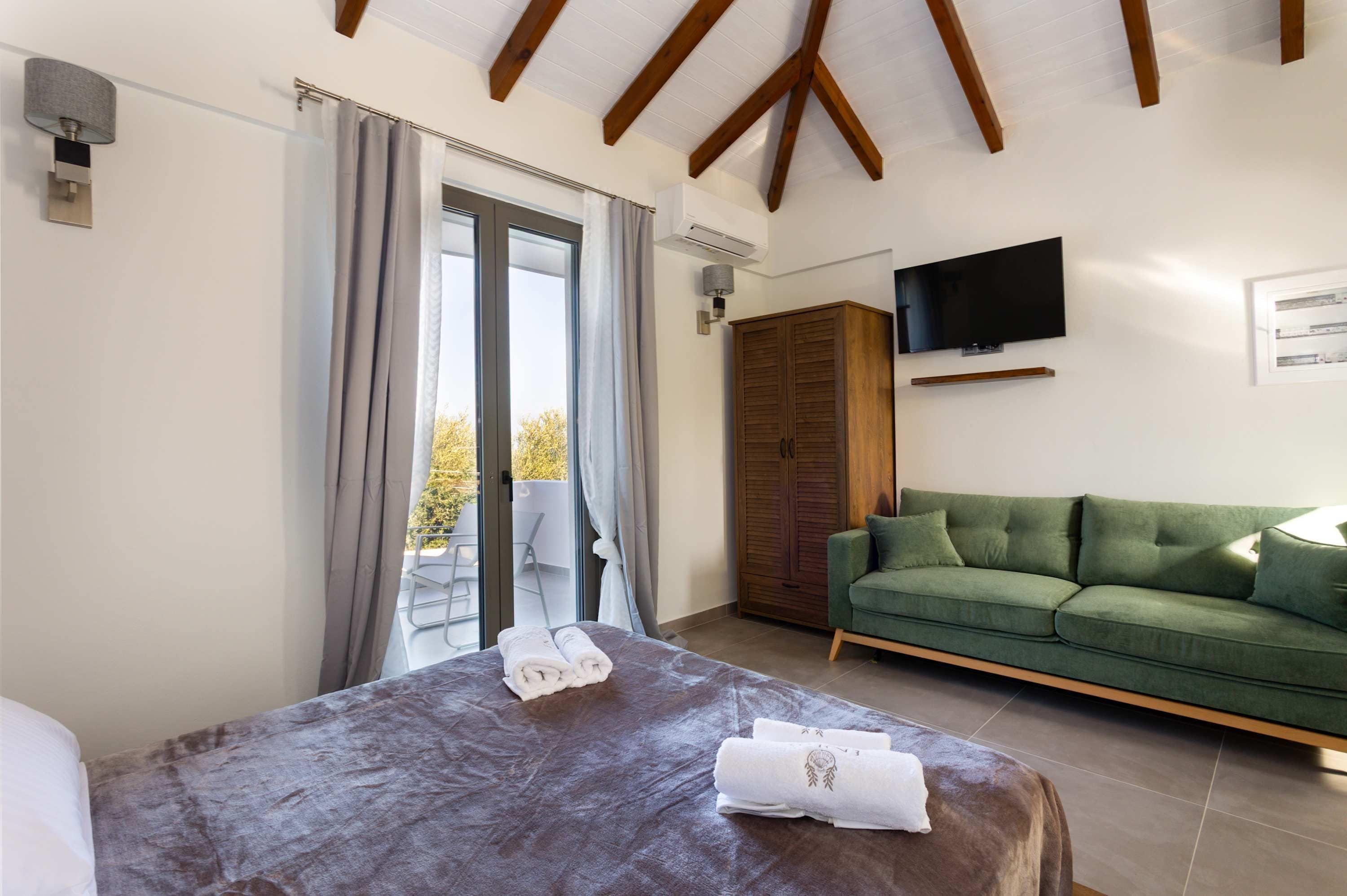 Quarto de hotel com cama, sofá verde, televisão e guarda-roupa.