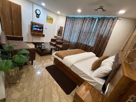 Quarto moderno com cama, televisão, escrivaninha e sofá.