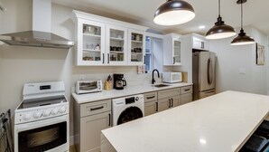 Uma cozinha moderna com armários brancos, coifa de aço inoxidável, forno embutido, lava-louças, micro-ondas e geladeira.