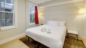 Quarto de hotel com uma cama grande, uma mesinha de cabeceira, uma janela com vista para árvores e uma cortina vermelha.