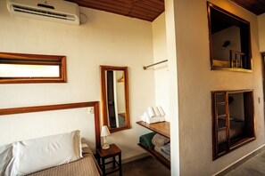 Quarto de hotel com cama, mesa de cabeceira com abajur, espelho, prateleira com toalhas e janela com vista para o exterior.