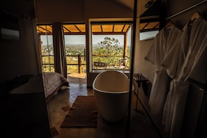 Quarto com cama, uma banheira grande e vista para o exterior.