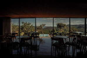 Uma área de refeições com mesas e cadeiras voltada para uma grande janela com vista para uma paisagem montanhosa.