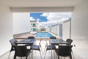 Espaço interior moderno com vista para piscina, com disposição de mesa e cadeiras, e céu claro.