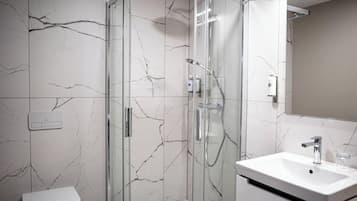 Uma casa de banho moderna com chuveiro de vidro, lavatório branco e sanita.