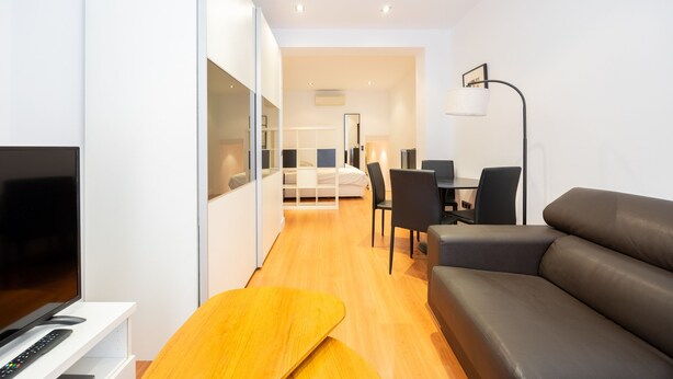 Uma sala de estar moderna com sofá, televisão, mesa de jantar com cadeiras e luminária.