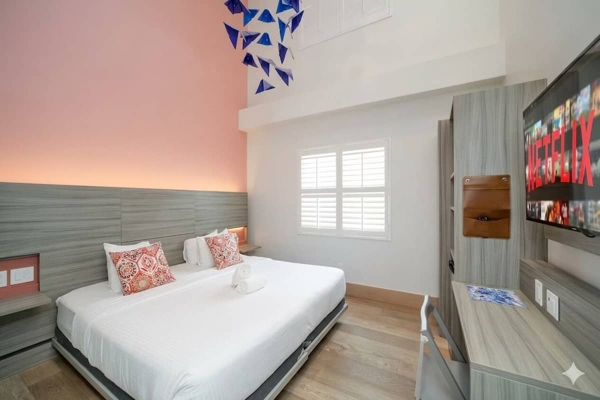 Quarto de hotel moderno com uma cama, televisão, janela e prateleira fixada na parede.