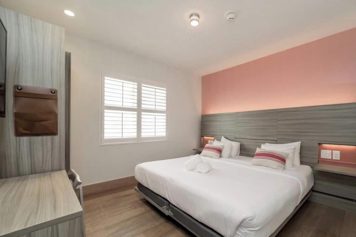 Quarto moderno com uma cama grande, mesas de cabeceira, um banco embutido, uma janela e uma prateleira fixada na parede.