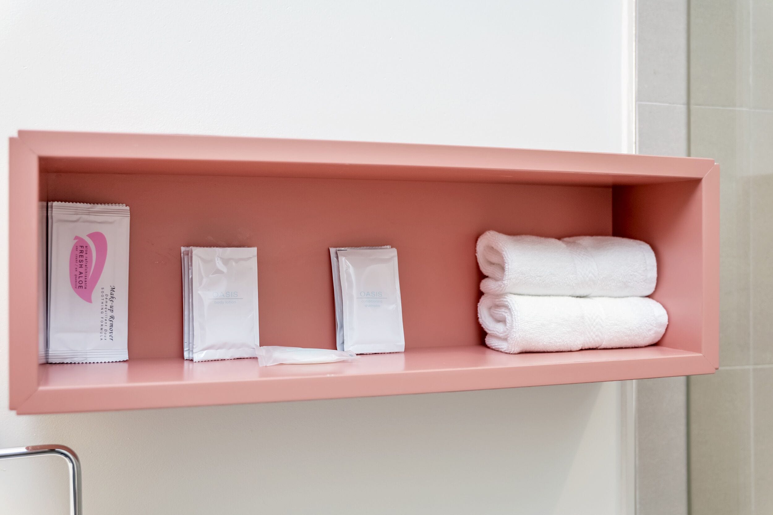 Estante rosa com produtos de higiene pessoal e toalhas dobradas em um banheiro.