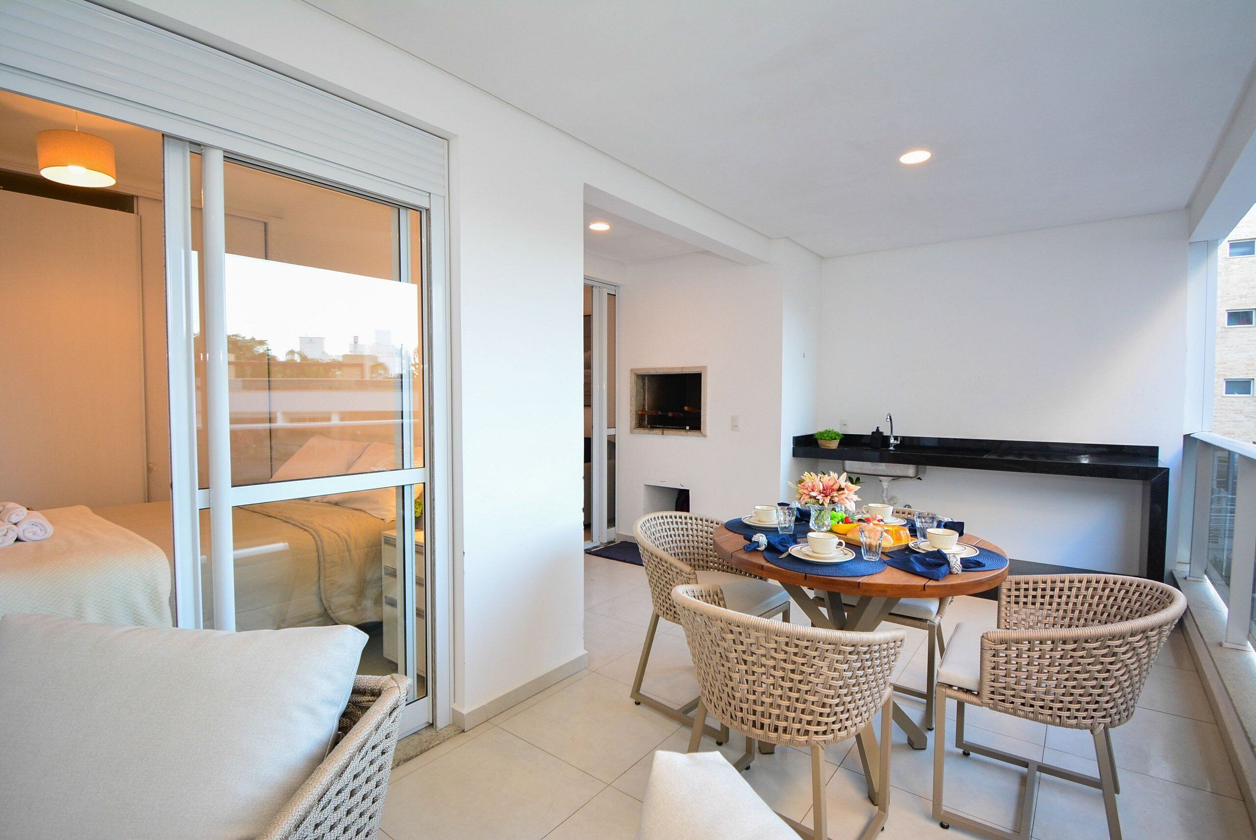 Quarto moderno com varanda, área de jantar com cadeiras de vime e cozinha.