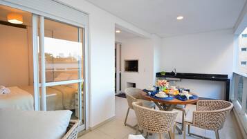 Quarto moderno com varanda, área de jantar com cadeiras de vime e cozinha.