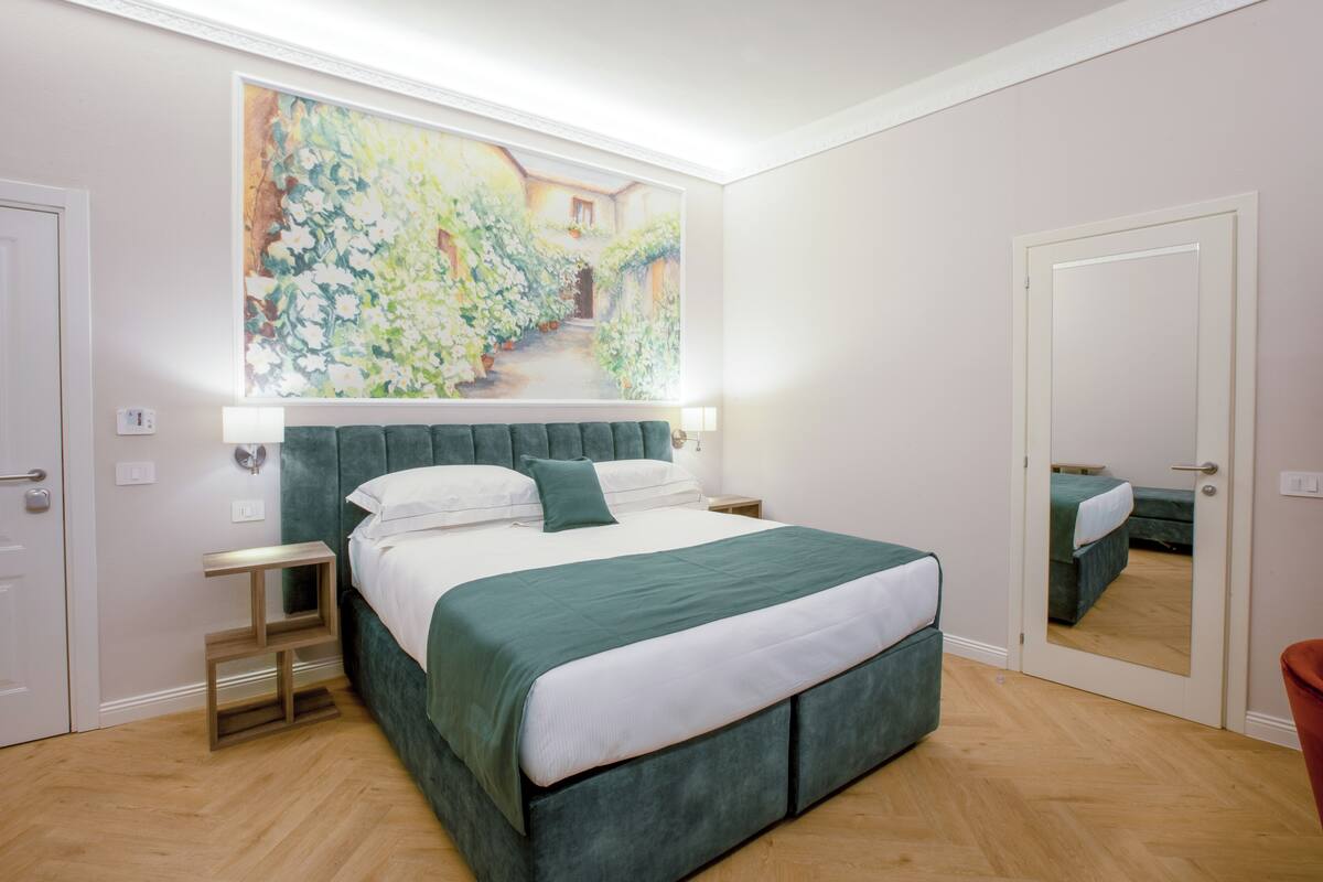 Quarto com cama grande, mesa de cabeceira, espelho e um quadro na parede.