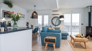 Uma sala de estar moderna com um sofá azul, uma mesa de centro de madeira e uma área de cozinha com um vaso de flores.